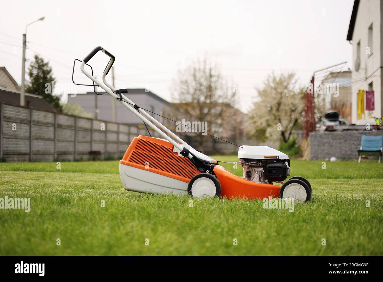 Modern orange-grey electric lawn mower on bright lush green lawn at ...