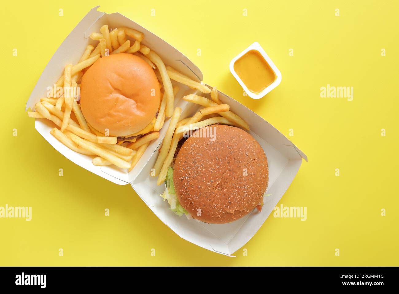 Open cardboard box with burgers and french fries on a yellow background ...