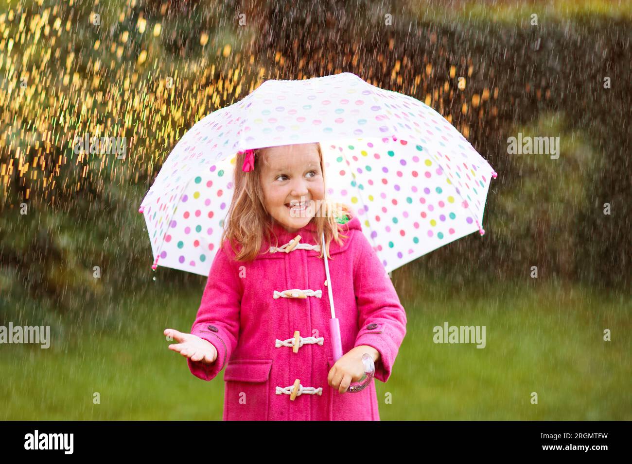 Little girl playing in rainy summer park. Child with colorful rainbow ...