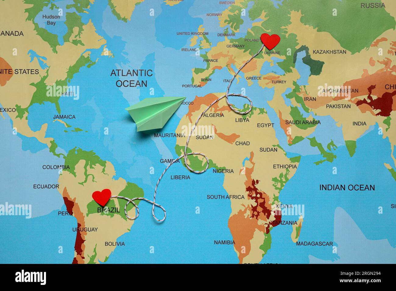 Paper plane and decorative cord between two red hearts on world map ...