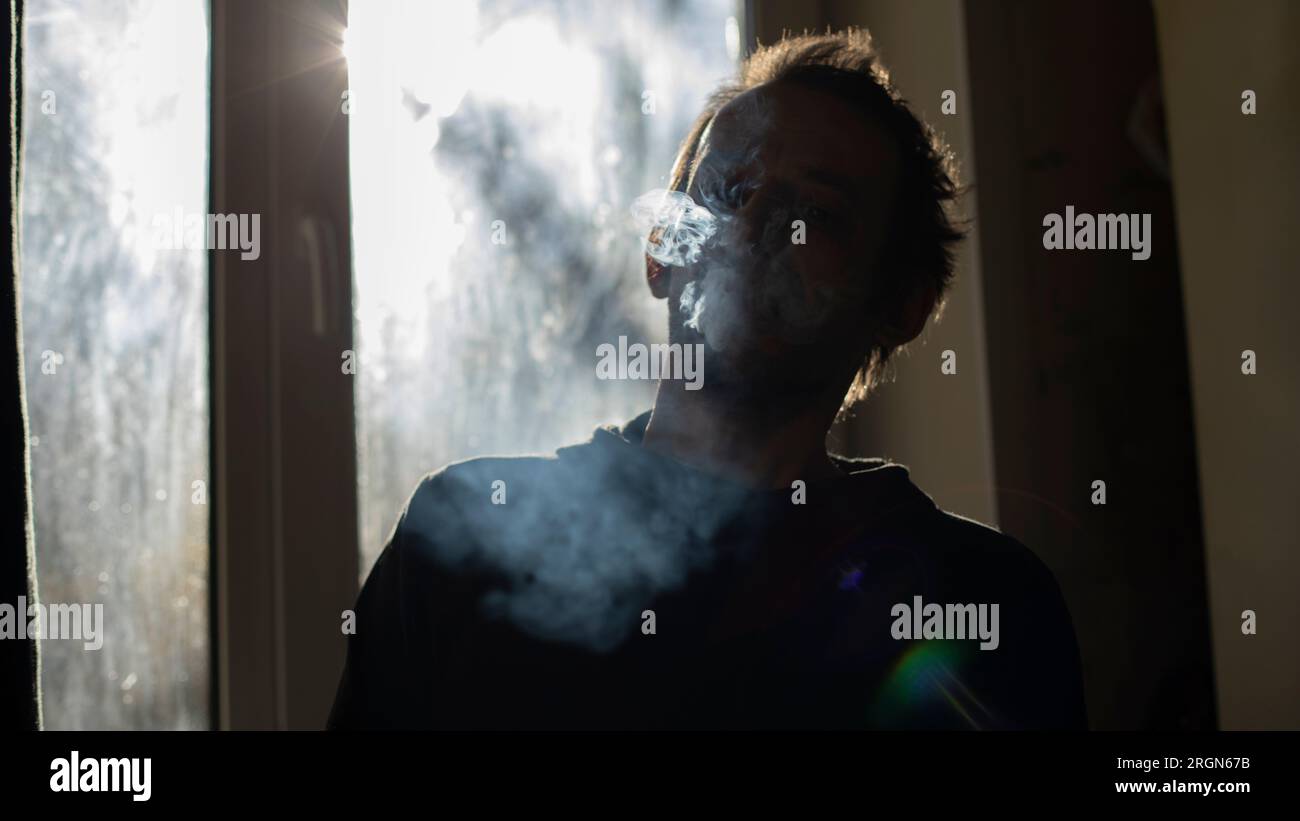 Guy smokes in morning. Man in background of window in smoke. Smoke from ...