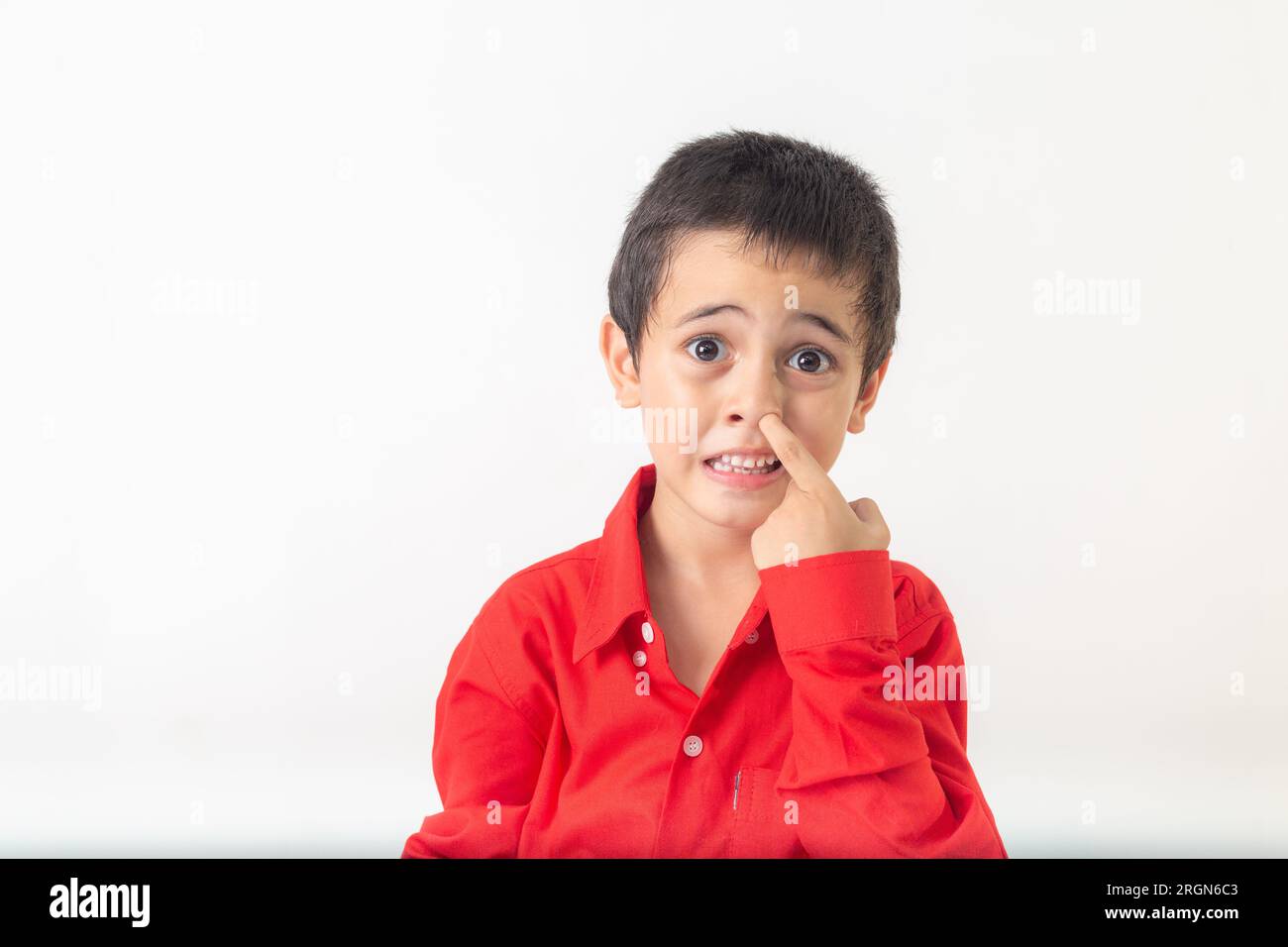 cute boy making a sly face. A cute looking boy in a red shirt making a ...