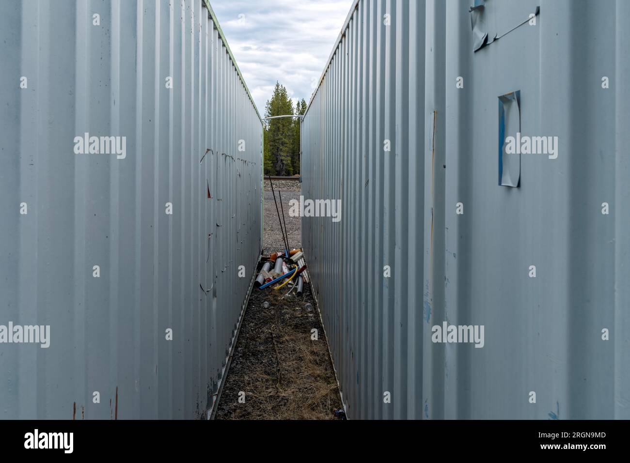 Junk piled up between two metal; container buildings Stock Photo - Alamy