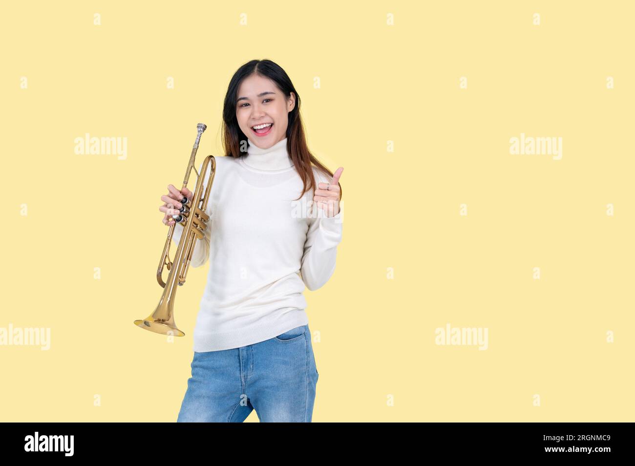 A cheerful and talented Asian female musician with a trumpet shows her ...