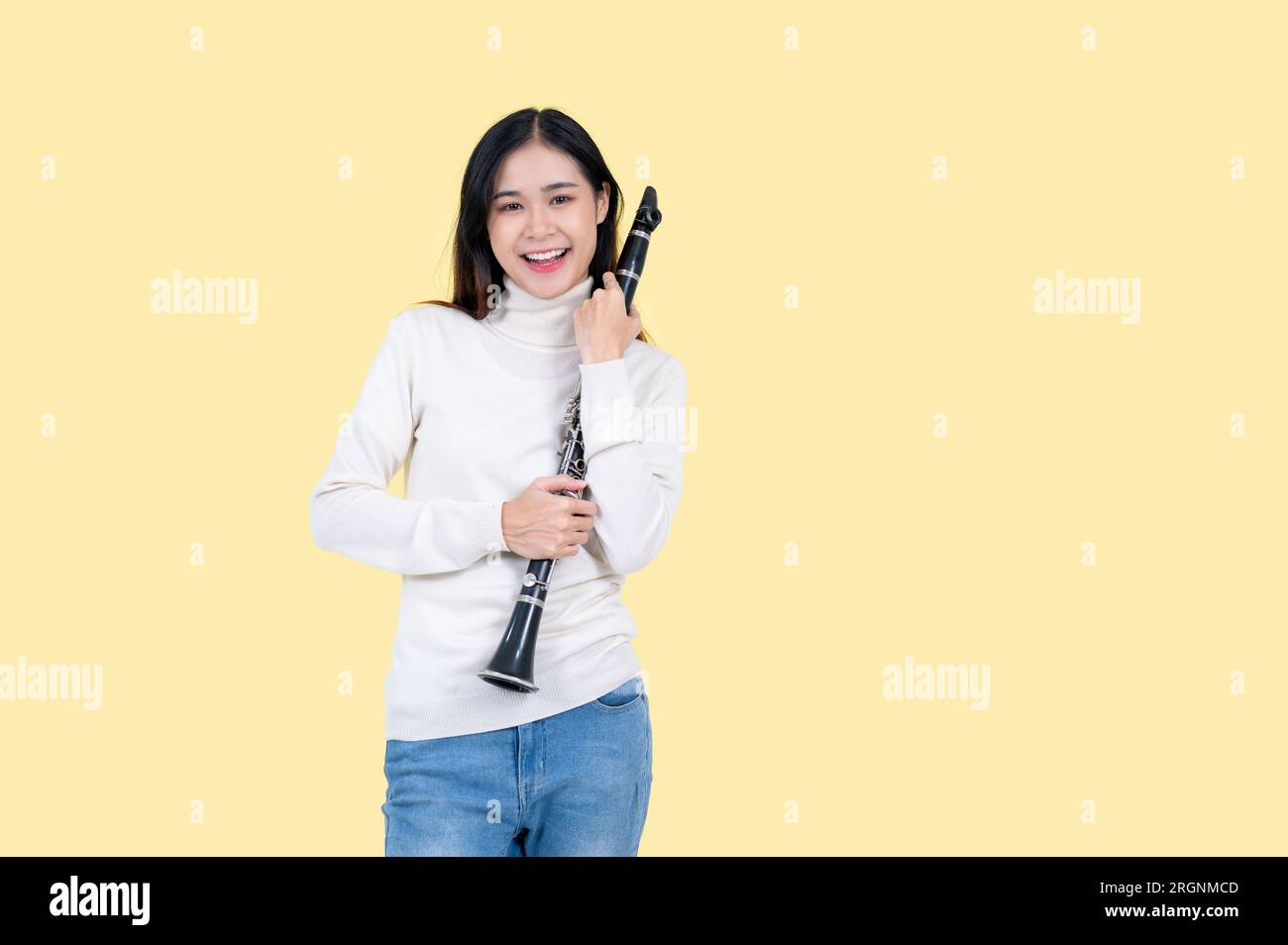 An attractive, smiling Asian female musician with a clarinet stands ...