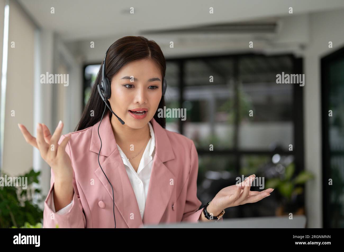 A professional and beautiful Asian female customer service or call-centre agent in headset is ...