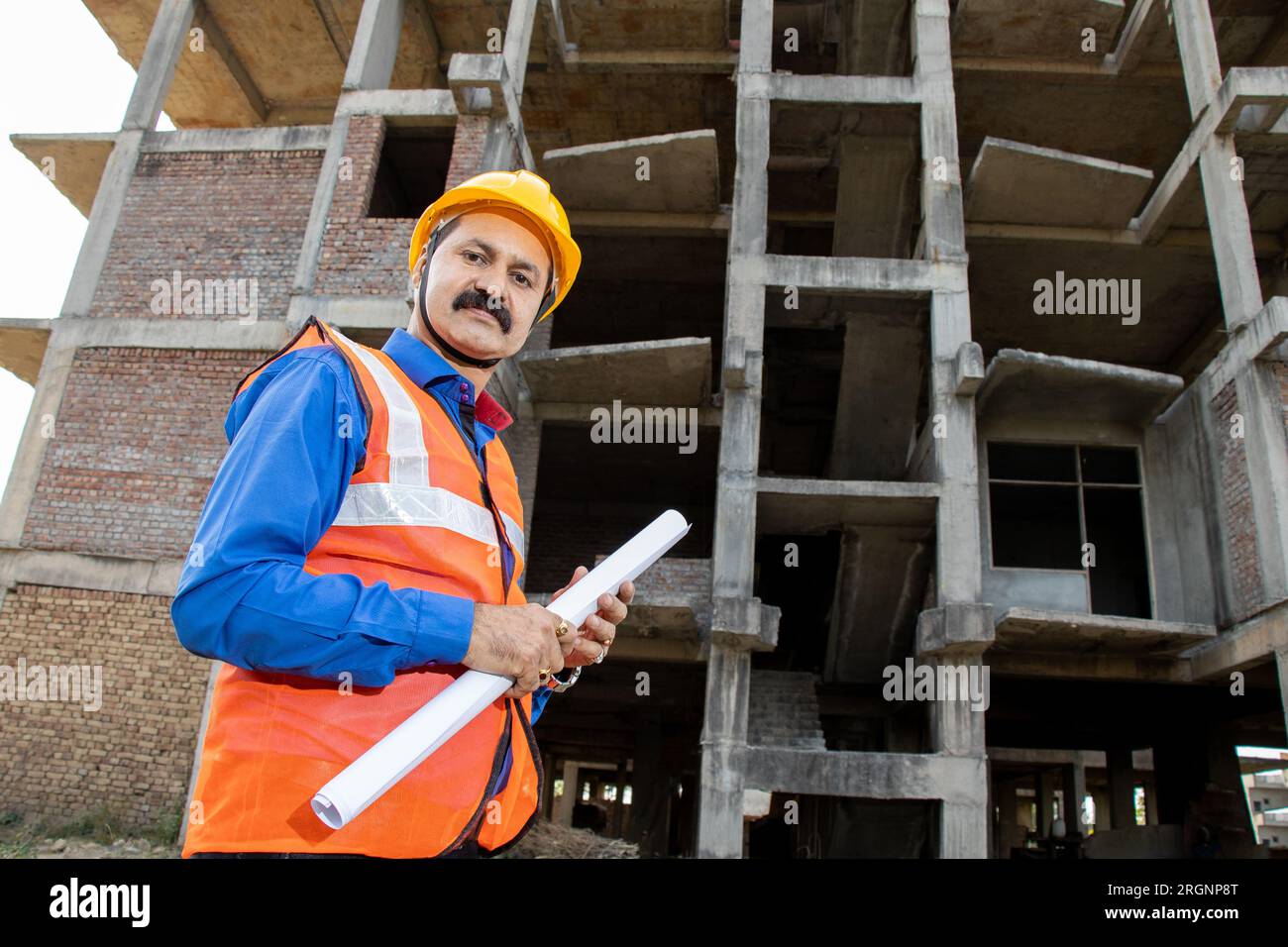 Mature Indian male civil engineer or architect wearing helmet and vest holding paperwork ...