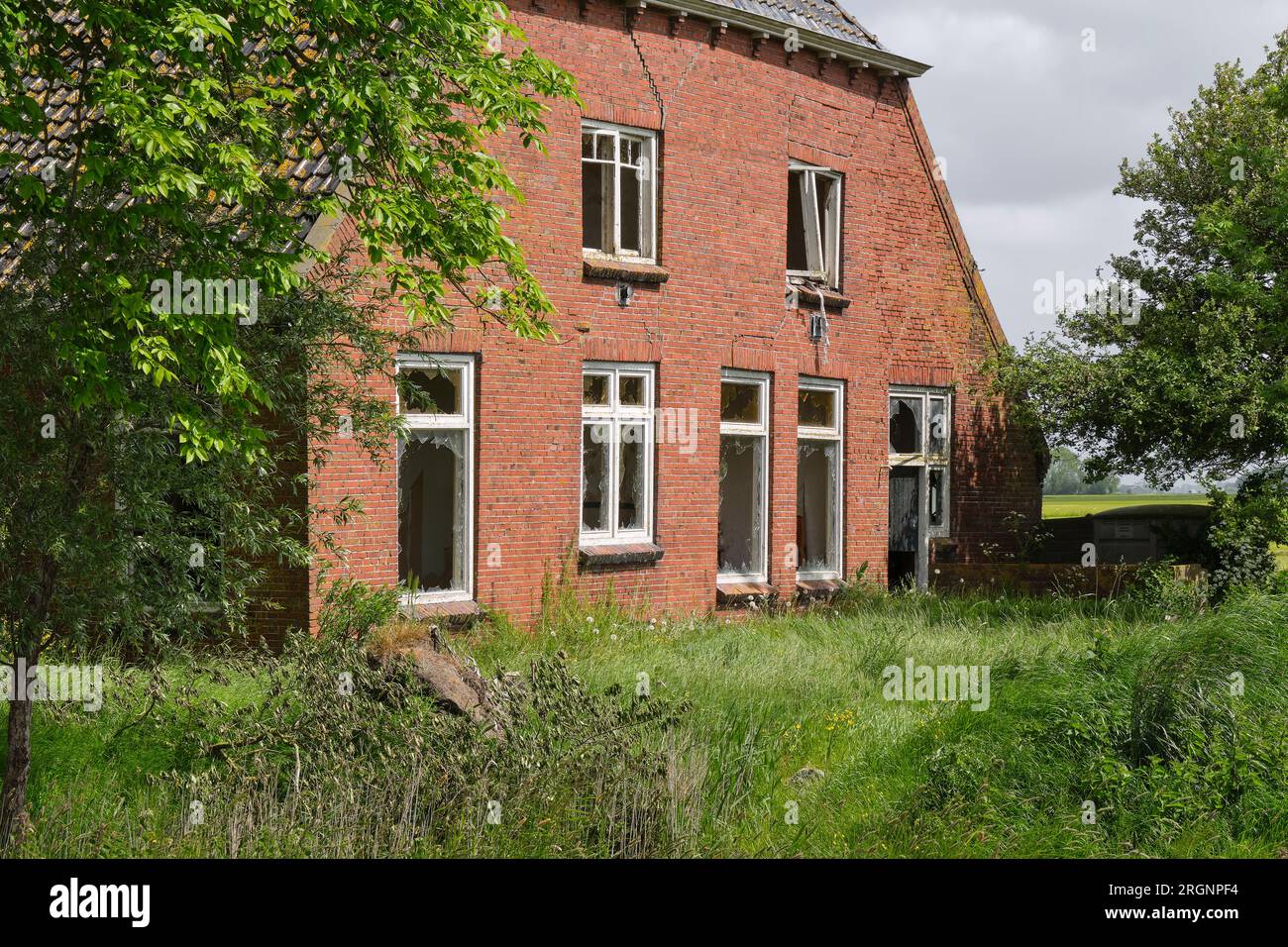 An abandoned and dilapidated farm house with red bricks and broken glass on a neglected terrain ...