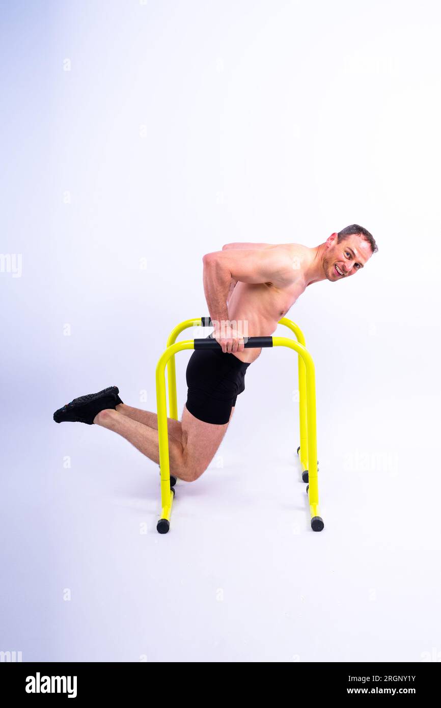 Young muscular man doing parallel bar exercises in dark white red ...
