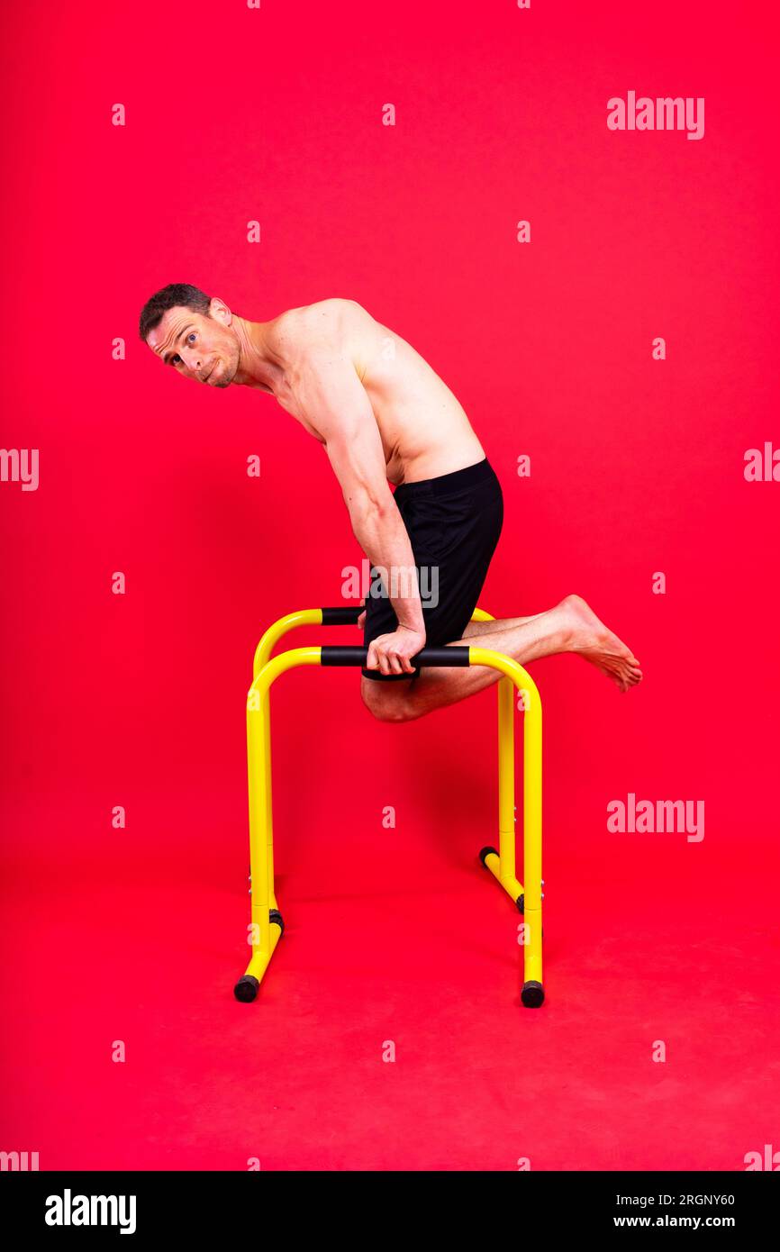 Young muscular man doing parallel bar exercises in dark white red ...