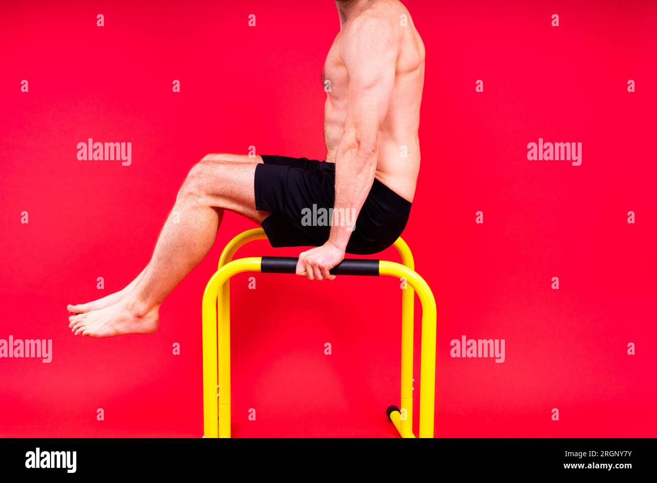Young muscular man doing parallel bar exercises in dark white red ...