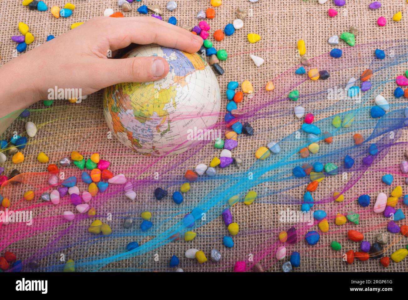 Model globe under hand amid little colorful pebbles Stock Photo - Alamy