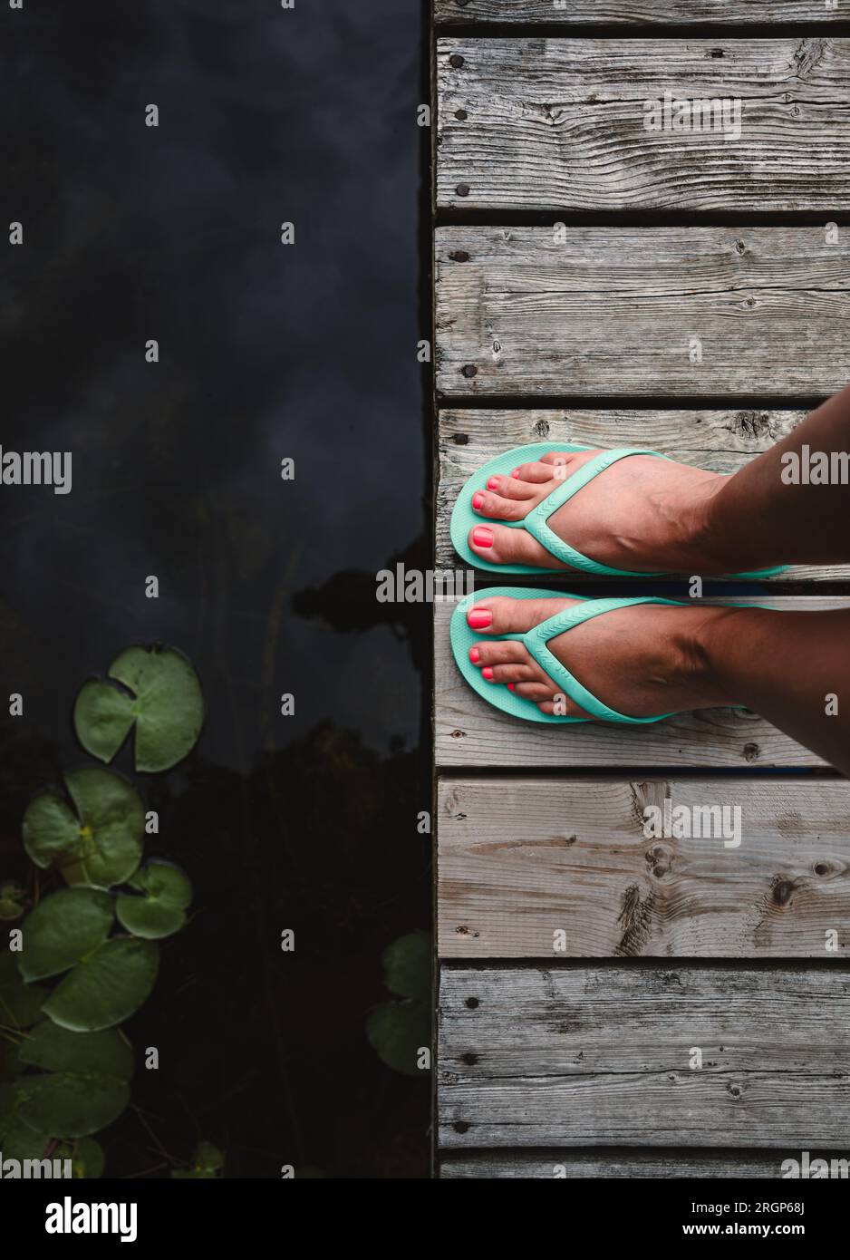 Overhead of woman's feet in sandals on worn wooden dock on lake Stock ...