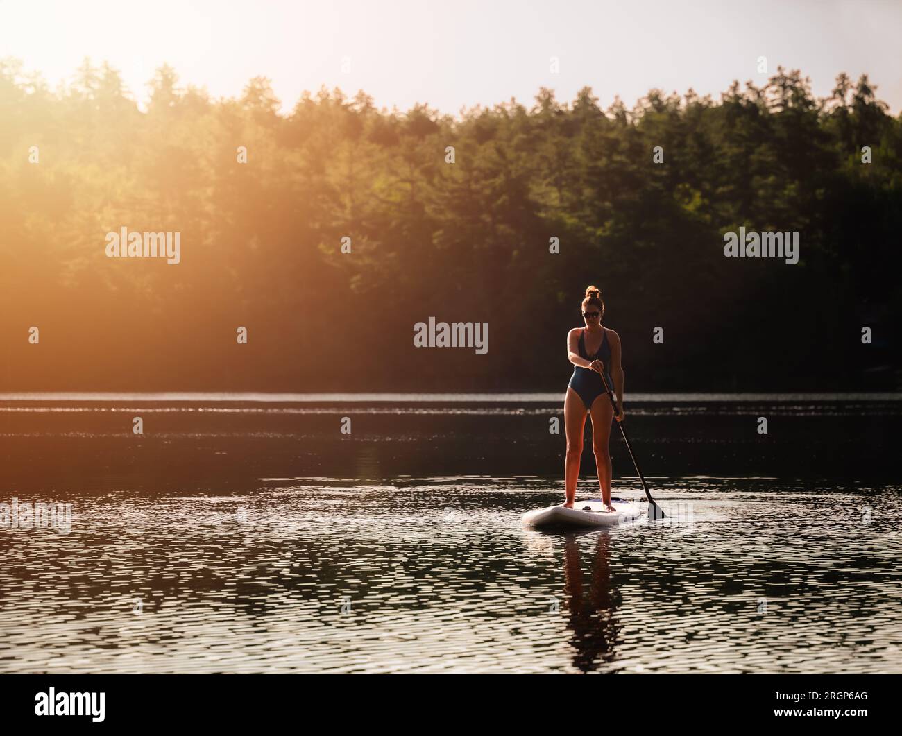 Woman in swim suit using paddleboard on lake in sunshine Stock Photo ...