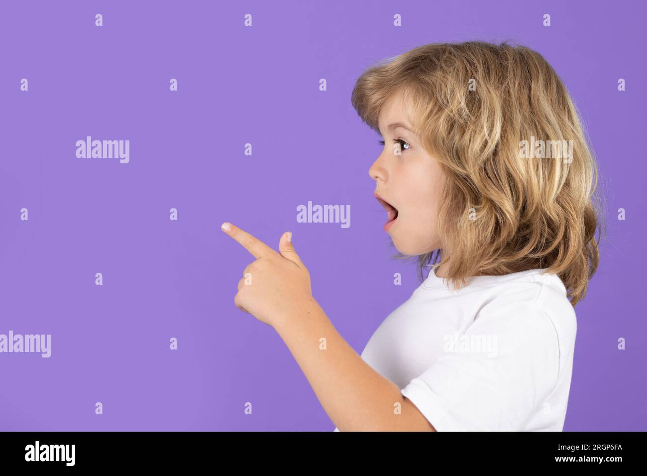 Surprised kid looking away, pointing finger on isolated studio ...