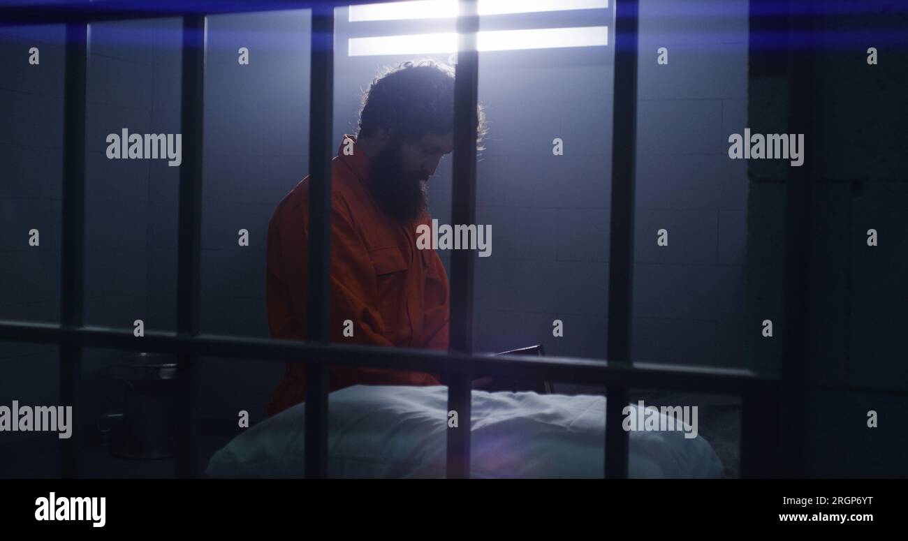Believing male prisoner in orange uniform kneels near the bed, prays to ...