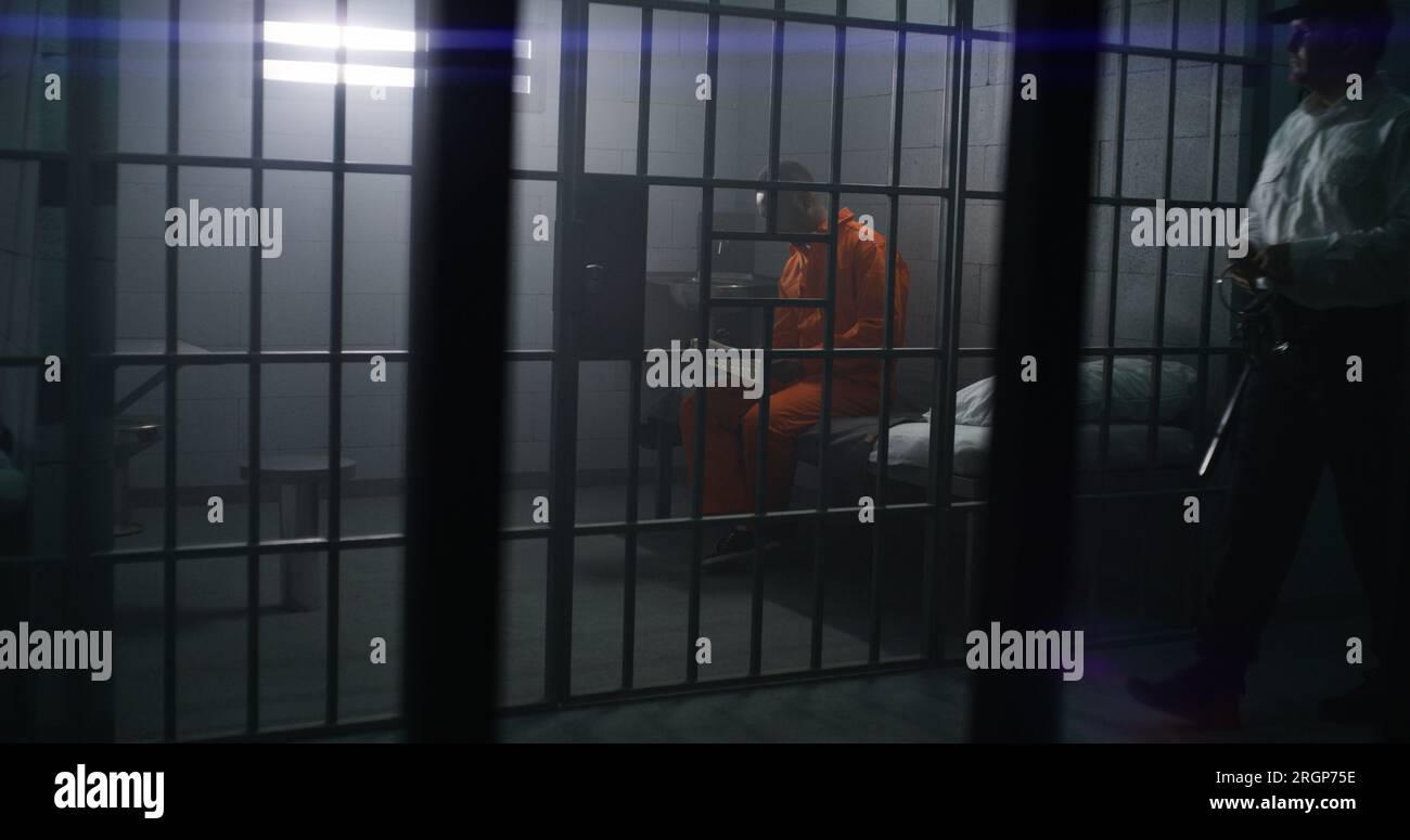African American prisoner in orange uniform sits on the bed, reads ...
