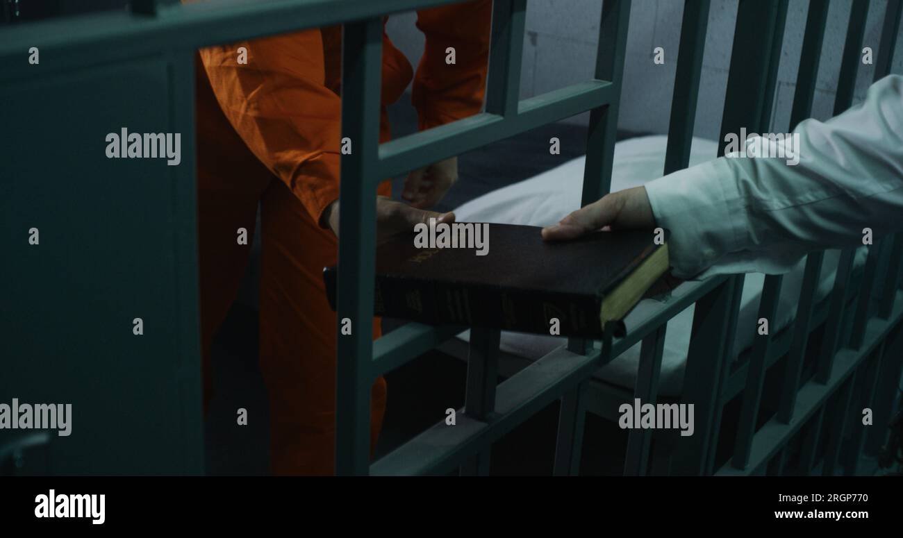 Prison officer gives Bible to male prisoner in orange uniform in prison ...