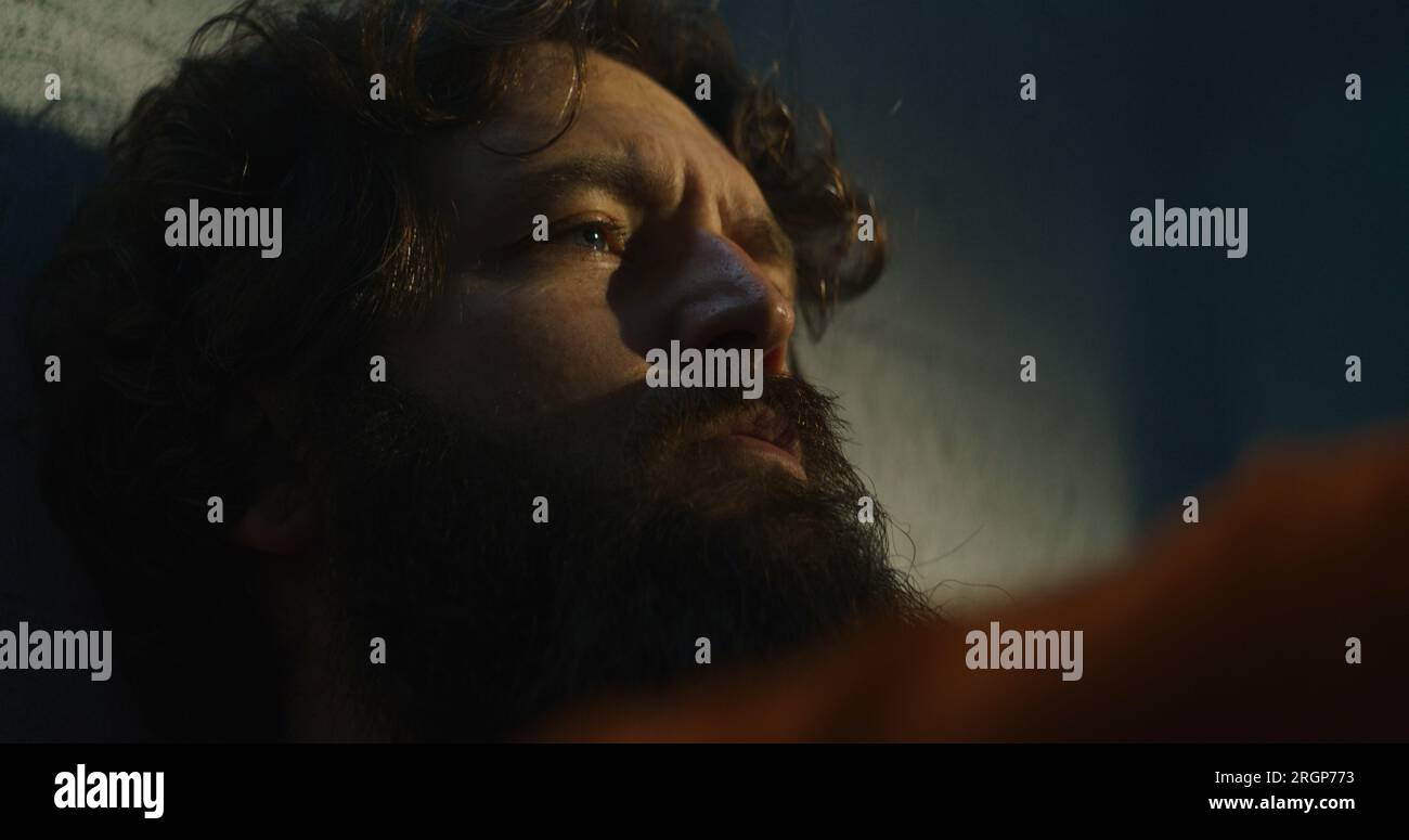 Depressed prisoner in orange uniform sits in prison cell, smokes ...