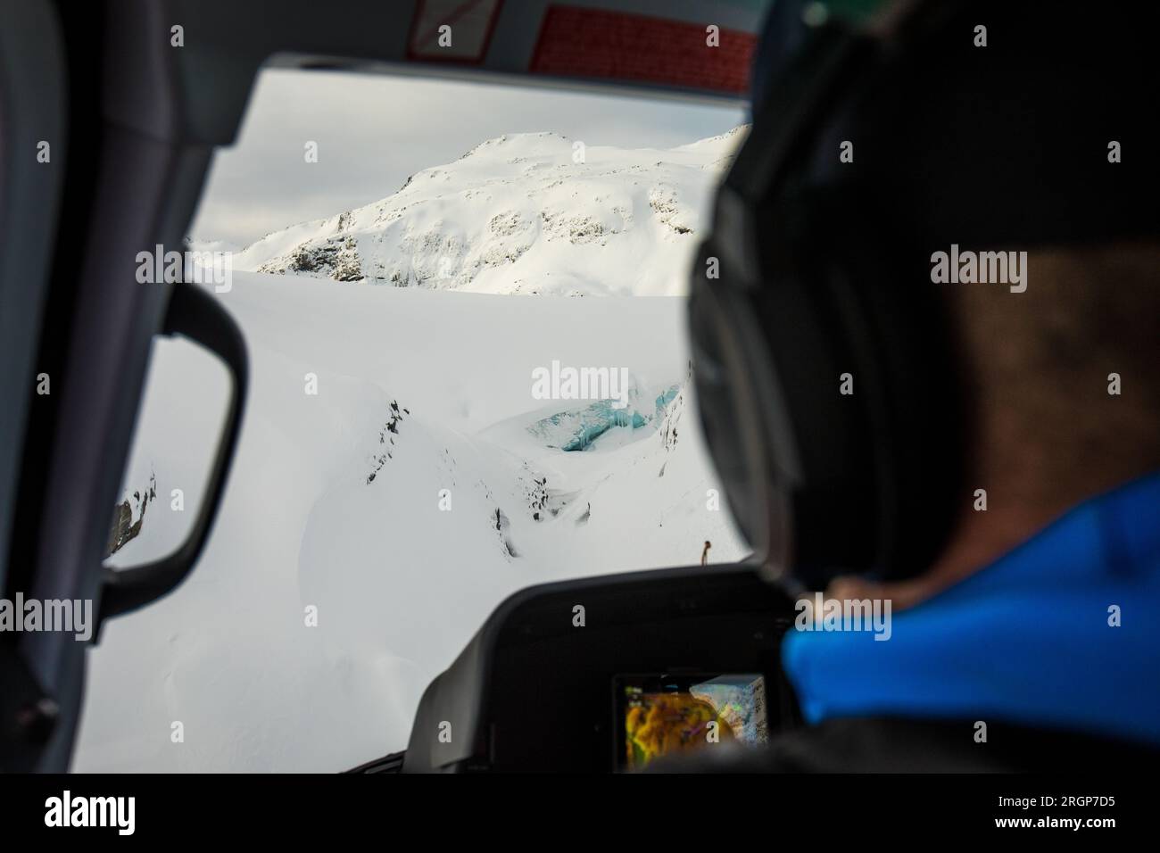 rear view of passenger looking out window of helicopter at glacier ...