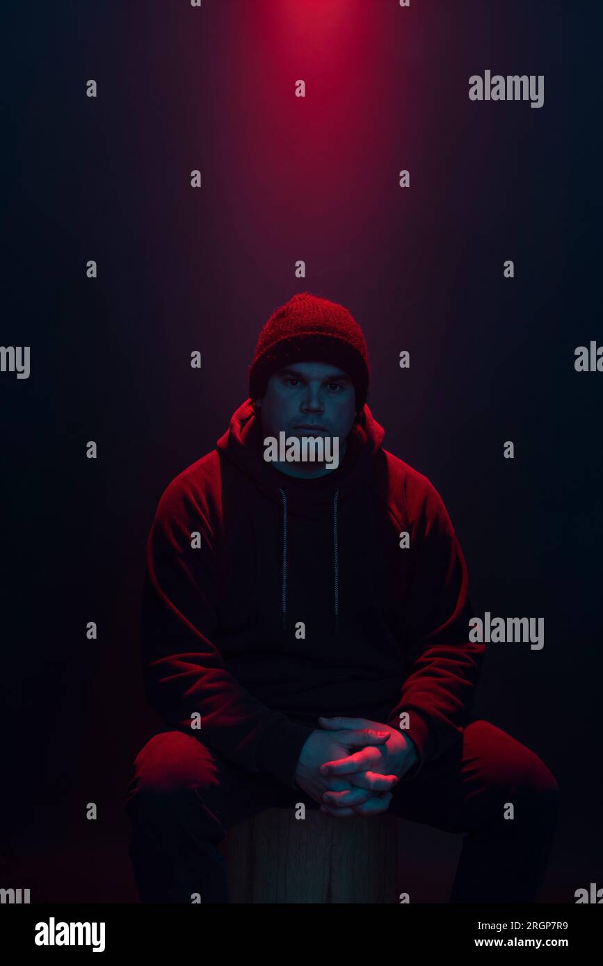 A man sitting on a stool is lit with a red light from above Stock Photo ...