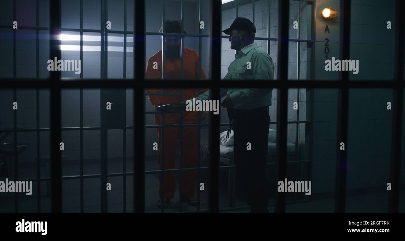 Prison officer gives Bible to male prisoner in orange uniform in prison ...