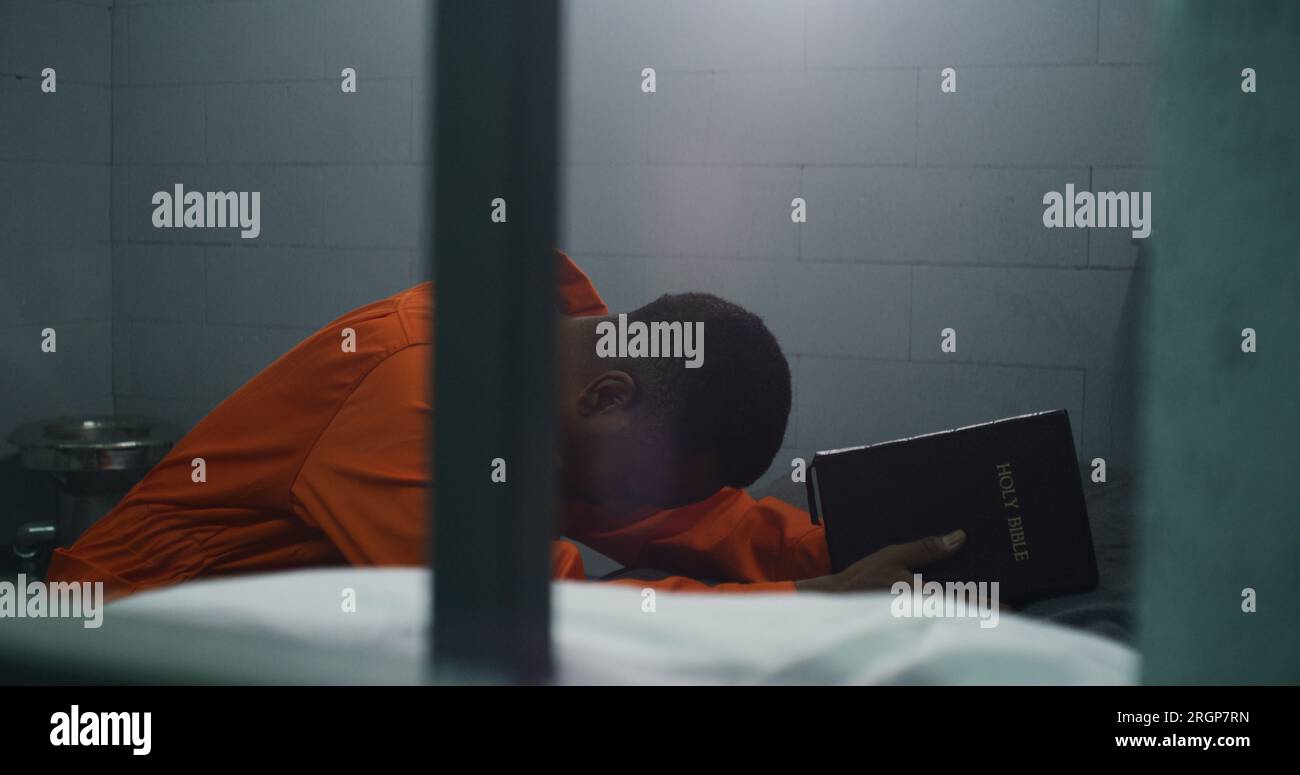 Religious African American prisoner in orange uniform kneels near the ...