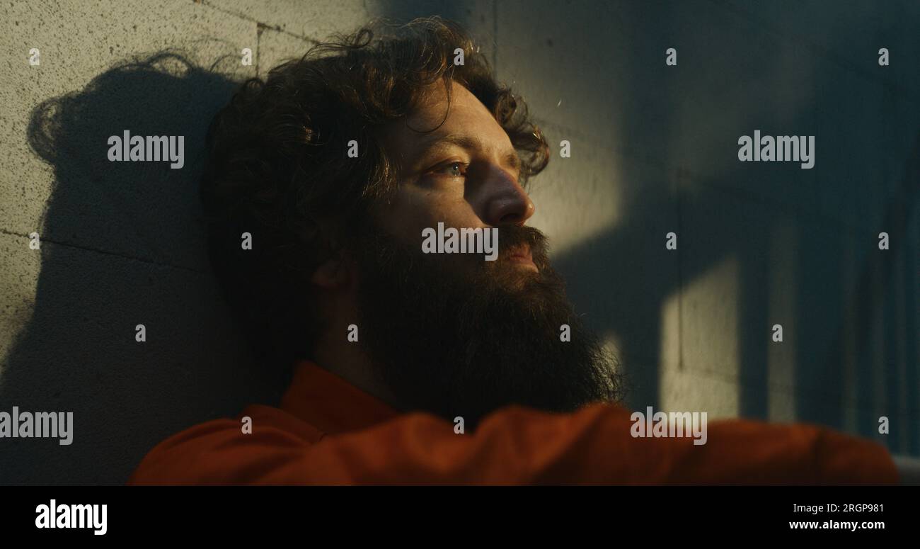 Depressed prisoner in orange uniform sits on bed, smokes cigarette in ...