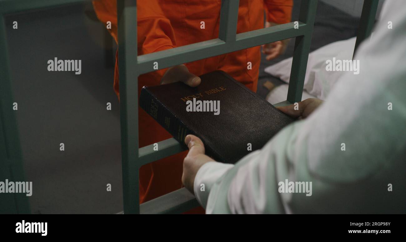 Prison officer gives Bible to male prisoner in orange uniform. Criminal ...