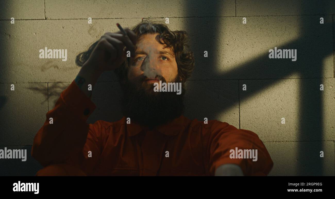 Depressed male prisoner in orange uniform sits in prison cell, lights ...