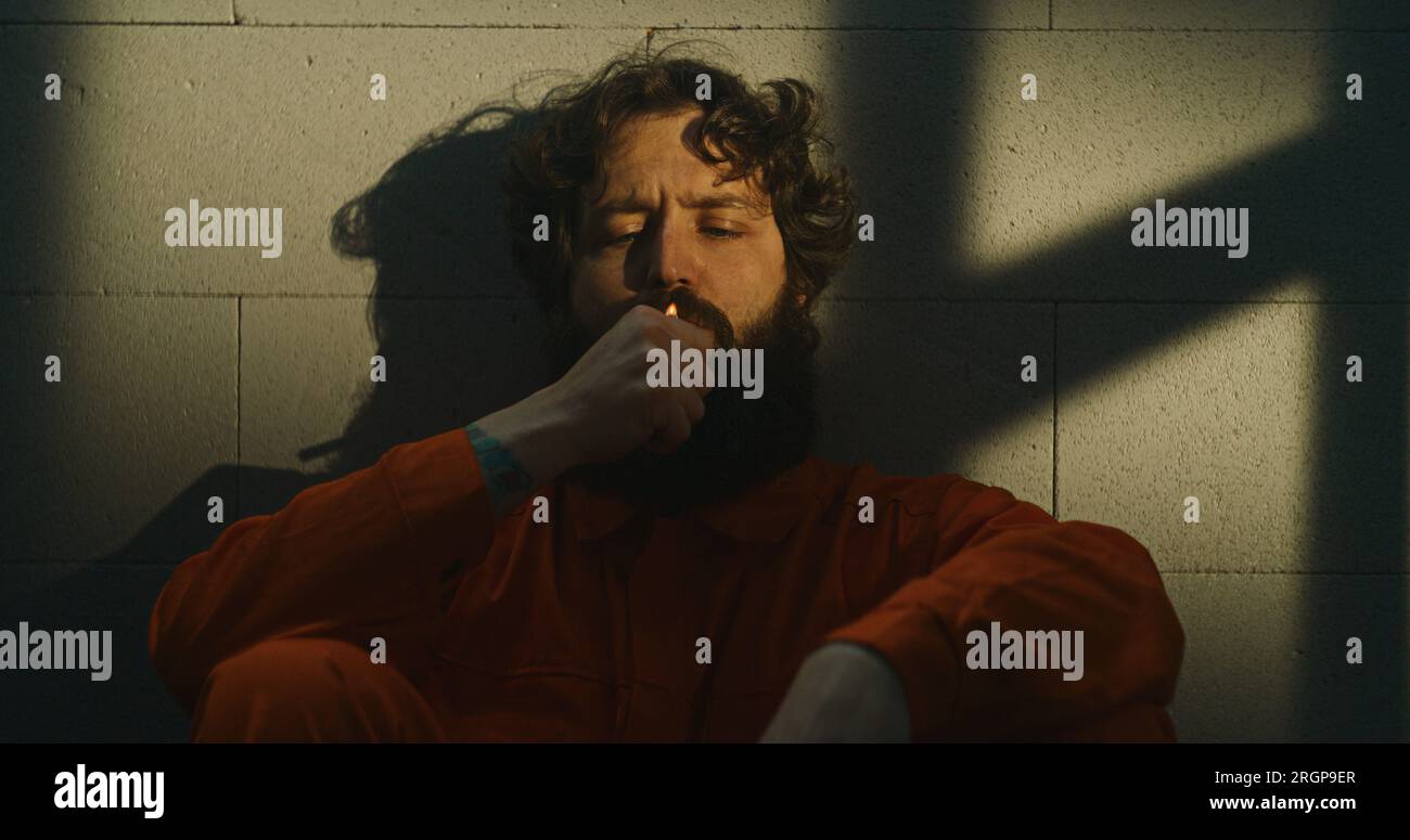 Depressed male prisoner in orange uniform sits in prison cell, lights ...