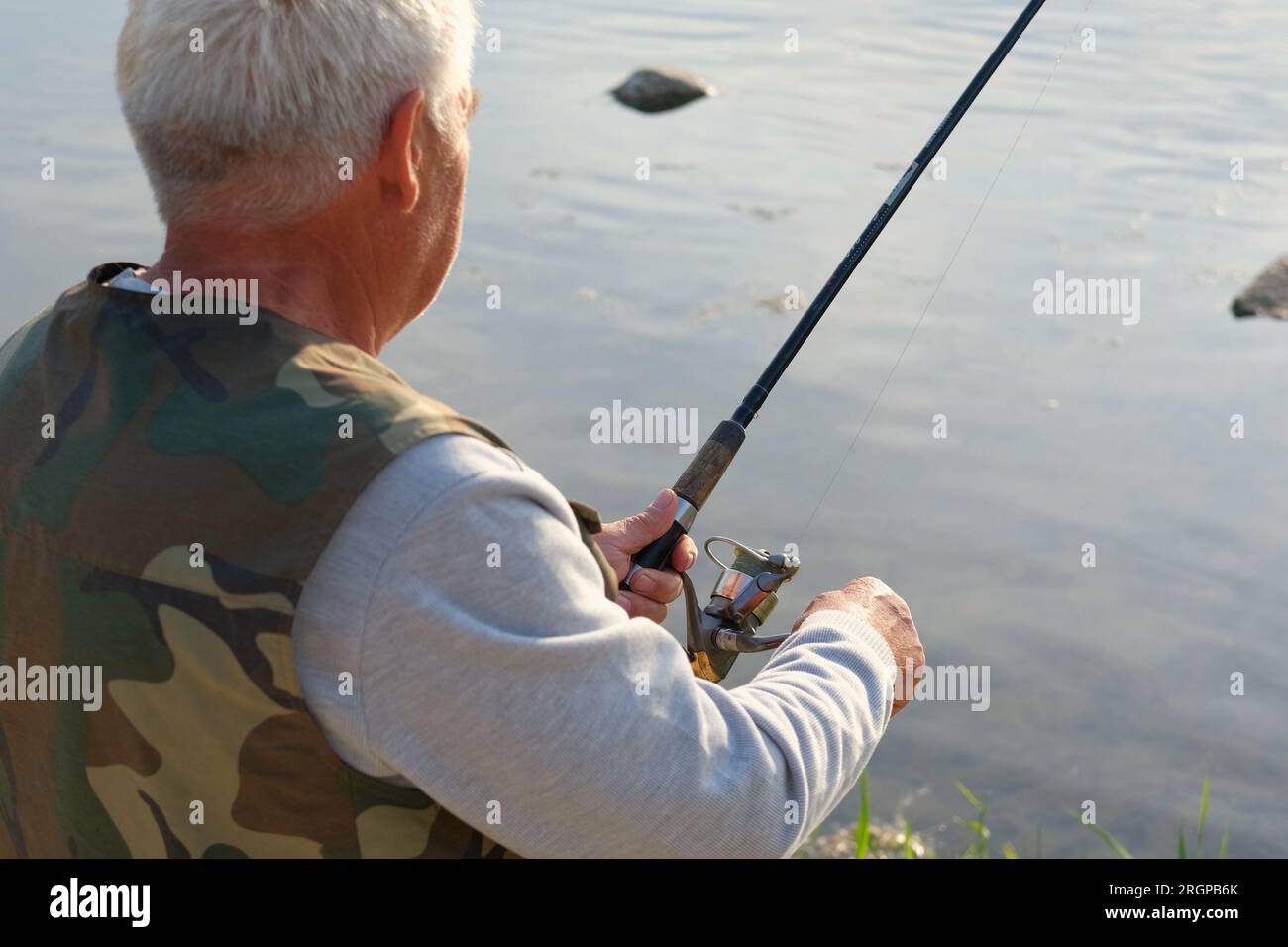 Old man fishing. Senior gray haired fisherman throws a spinning from ...