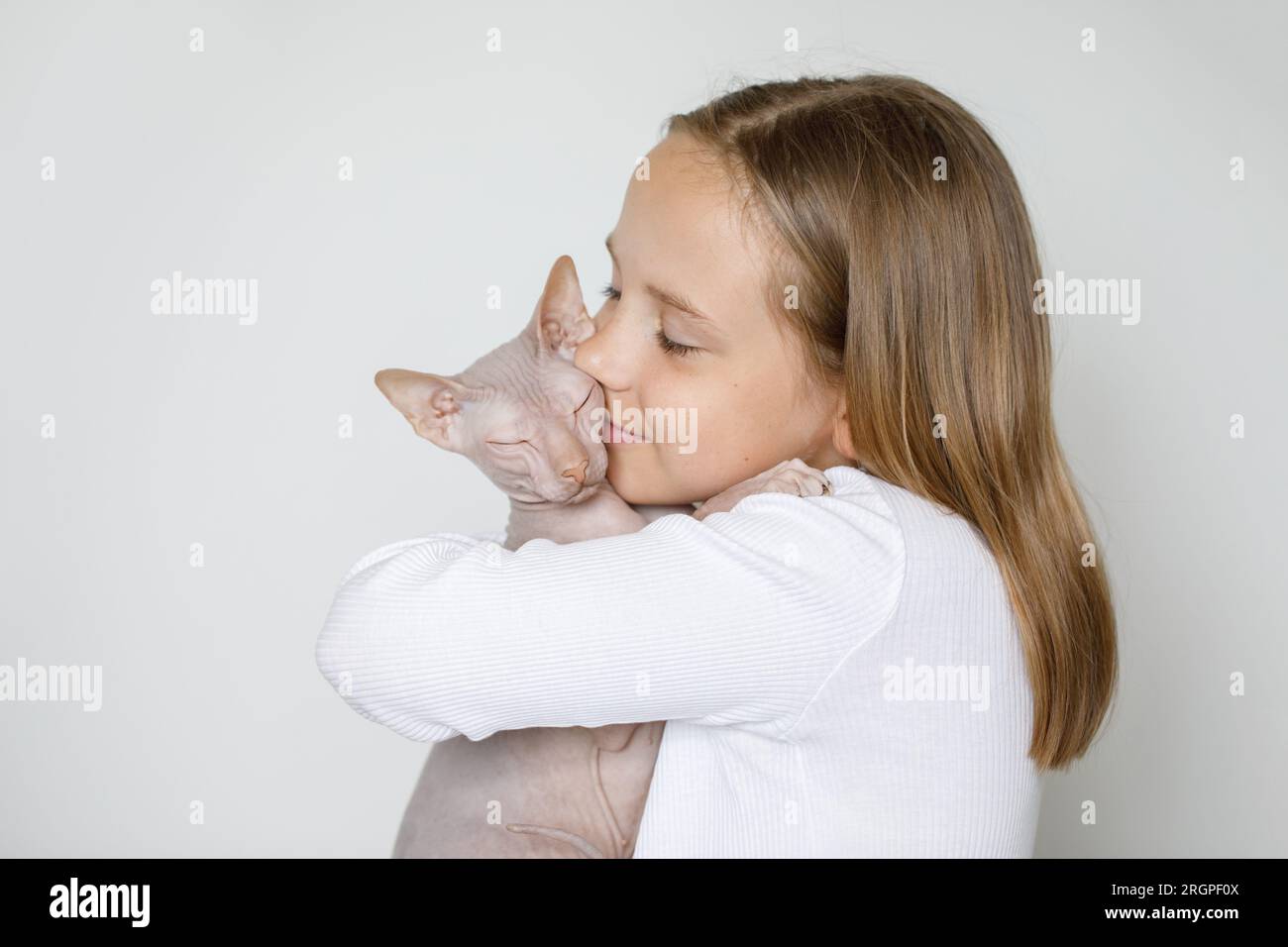 Beautiful child girl kissing cat pet on white studio wall background ...