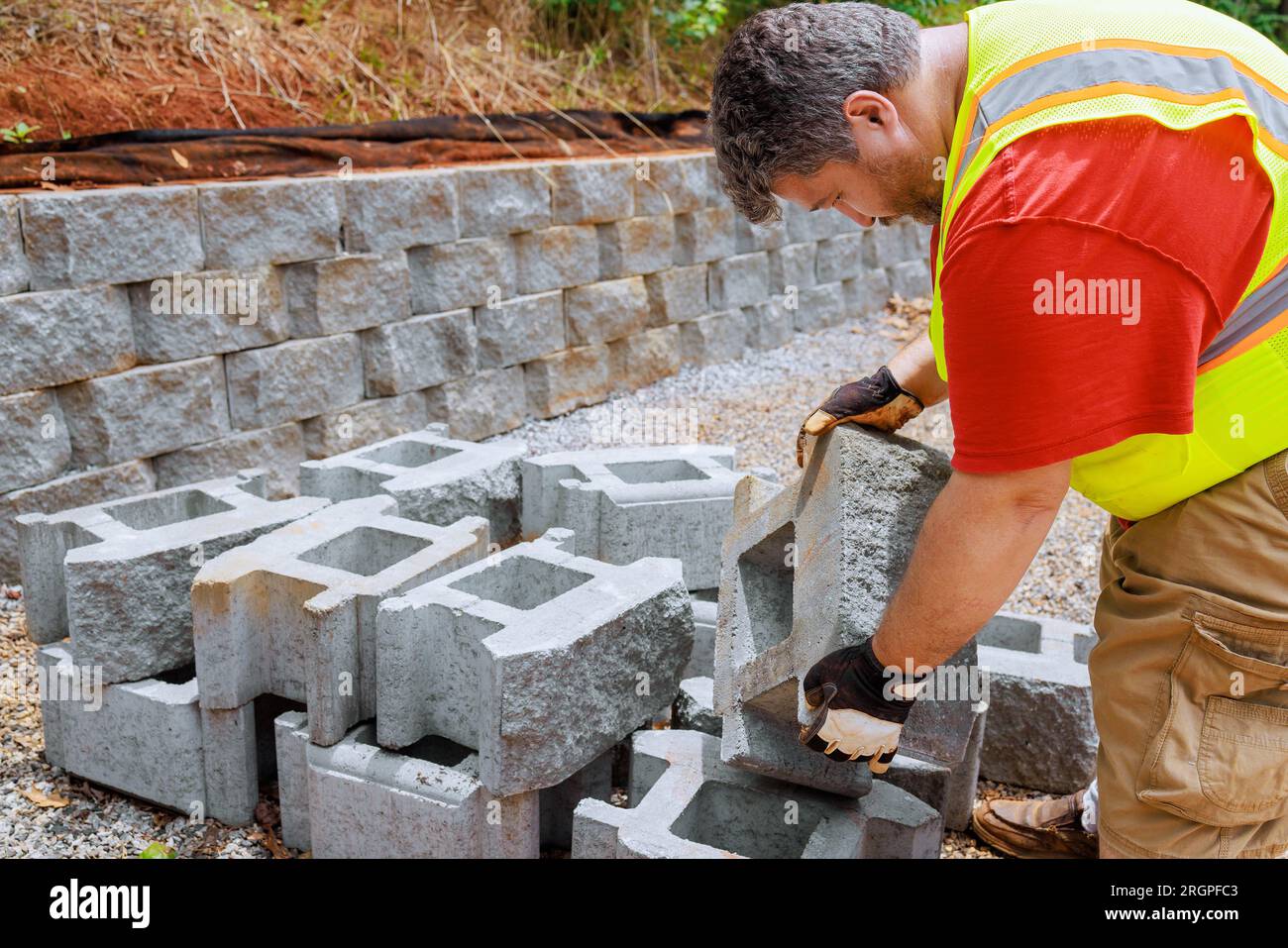 Construction worker lifts concrete block and places it on retaining ...