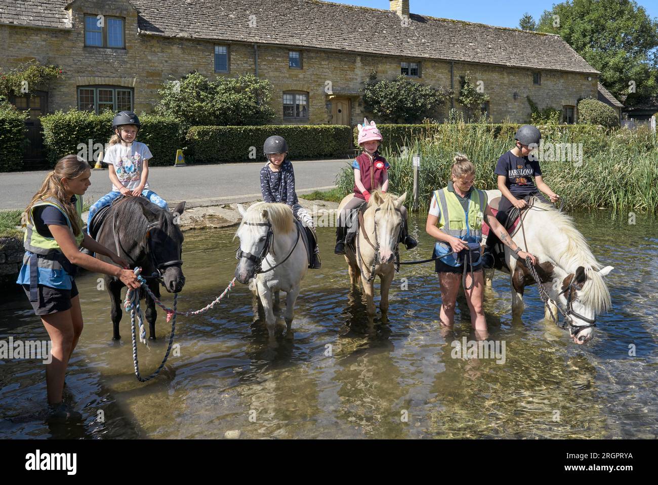 Children on a pony ride through the village stream at Lower Slaughter ...