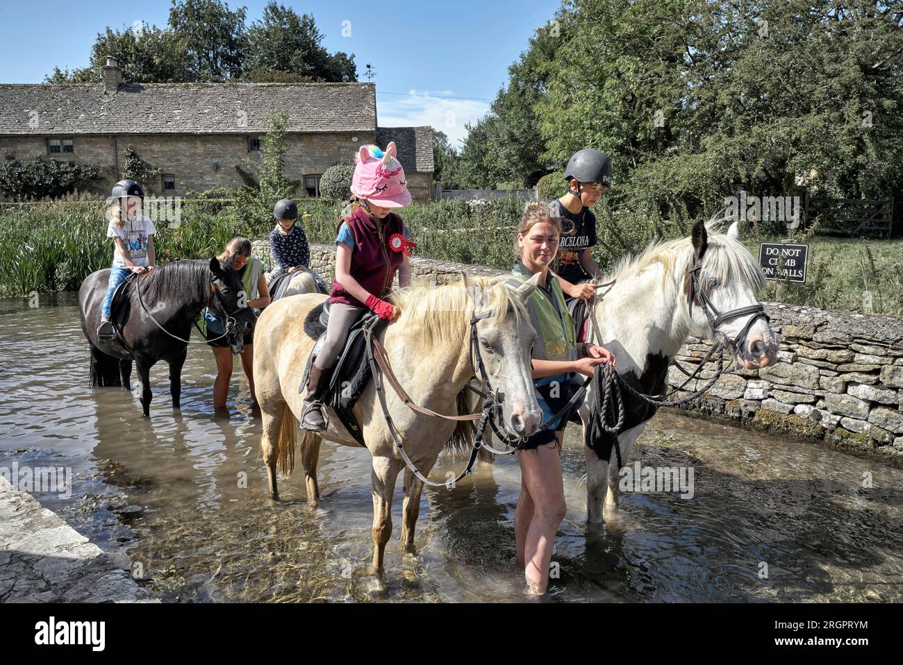 Children on a pony ride through the village stream at Lower Slaughter ...