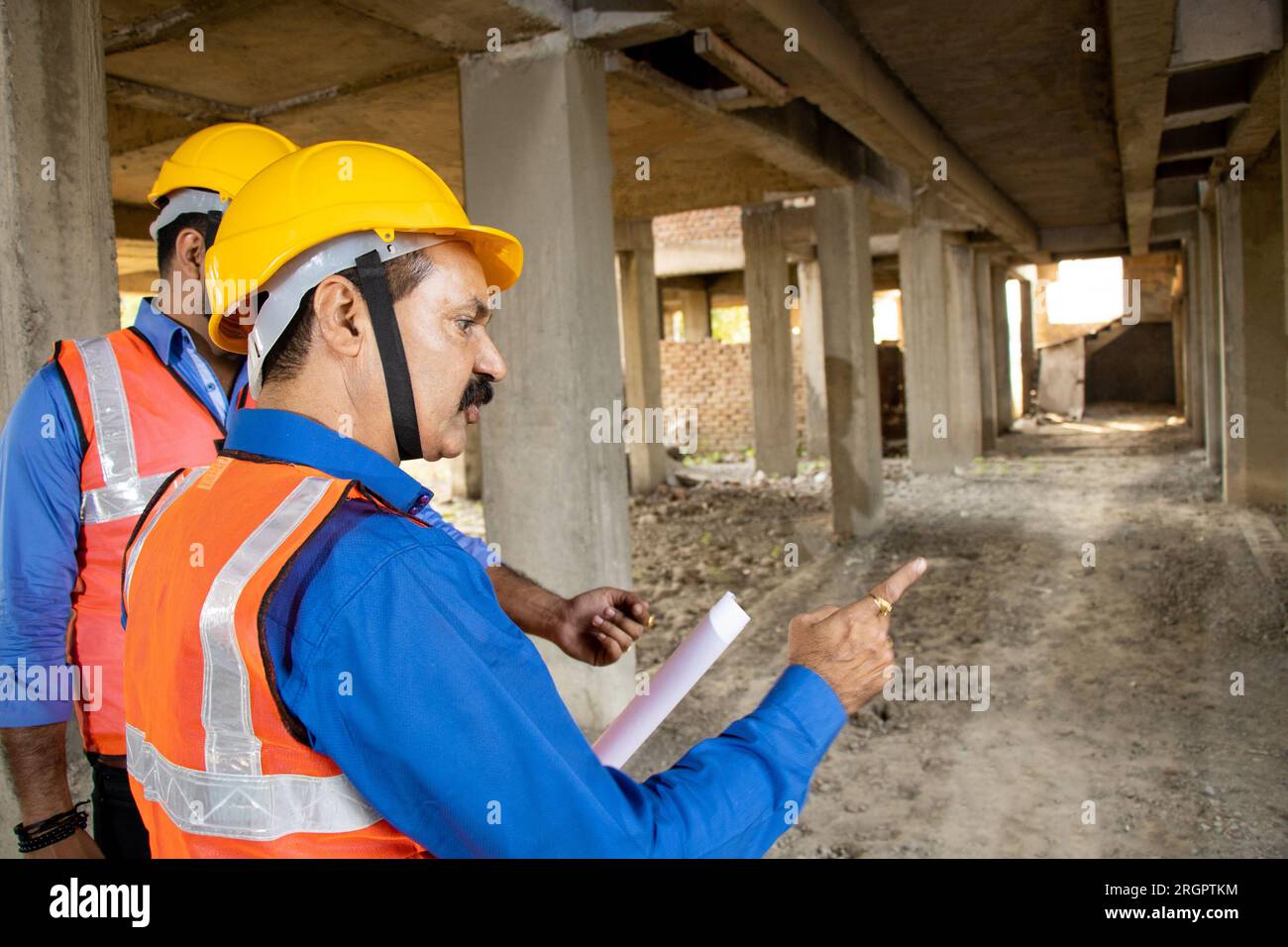 Two Indian female civil engineers or architect wearing helmet and vest working at construction ...
