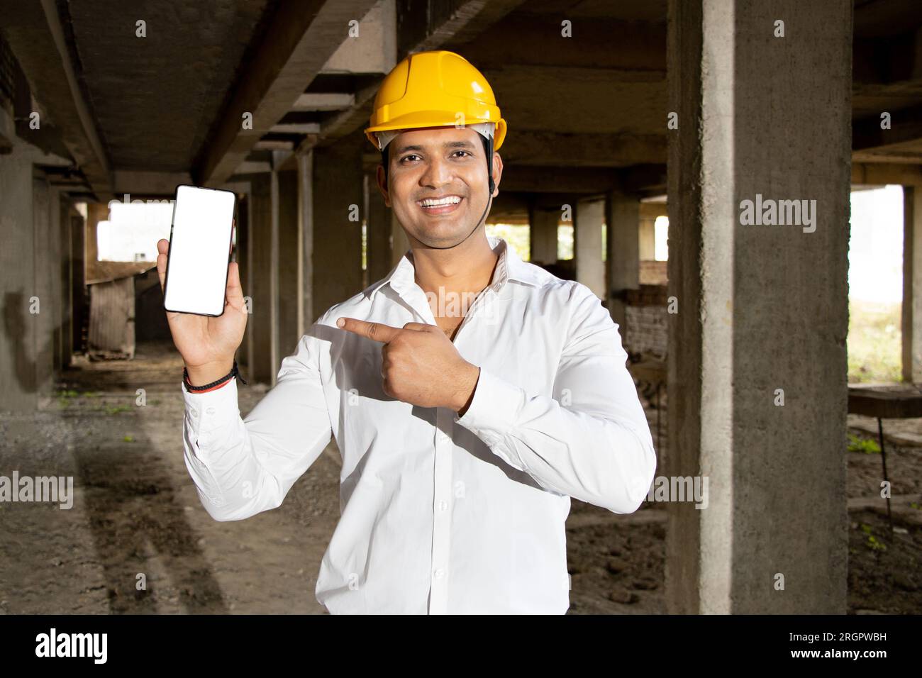 Portrait of happy young handsome Indian male civil engineer or architect wearing white shirt and ...