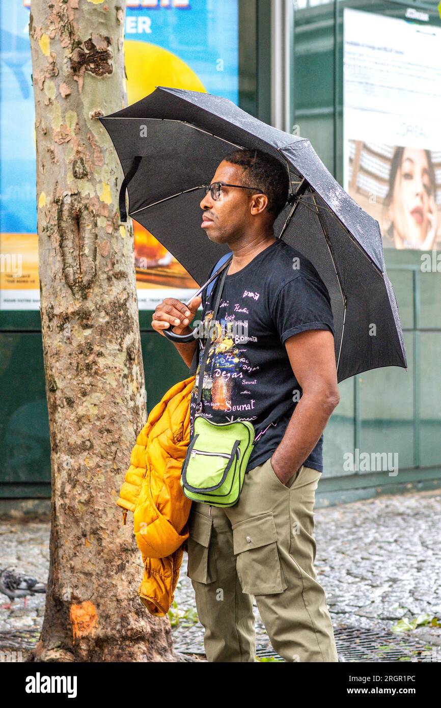 Black man sheltering under umbrella in rainy Paris, France Stock Photo ...