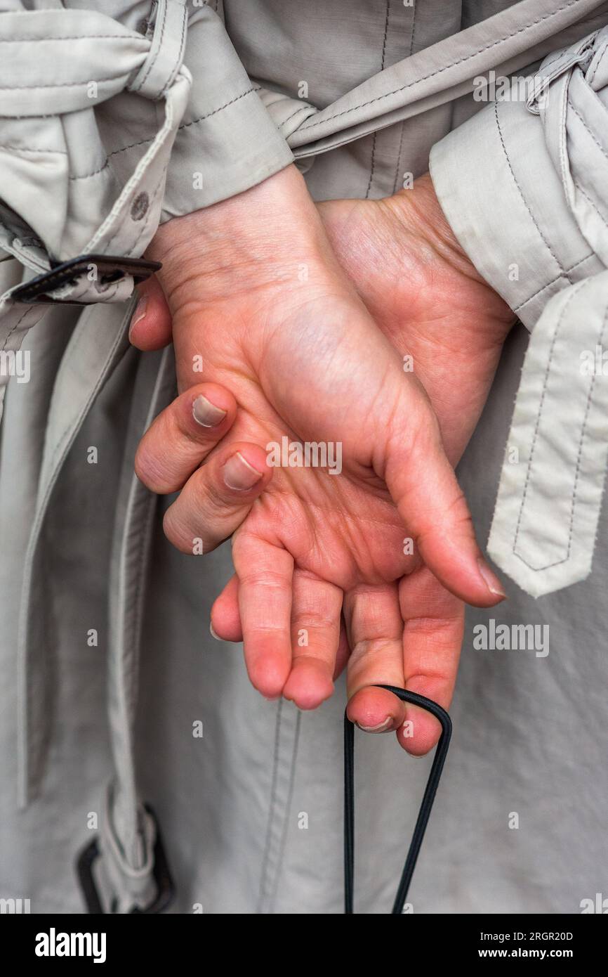 Young woman's hands held together behind back, holding cord Stock Photo ...