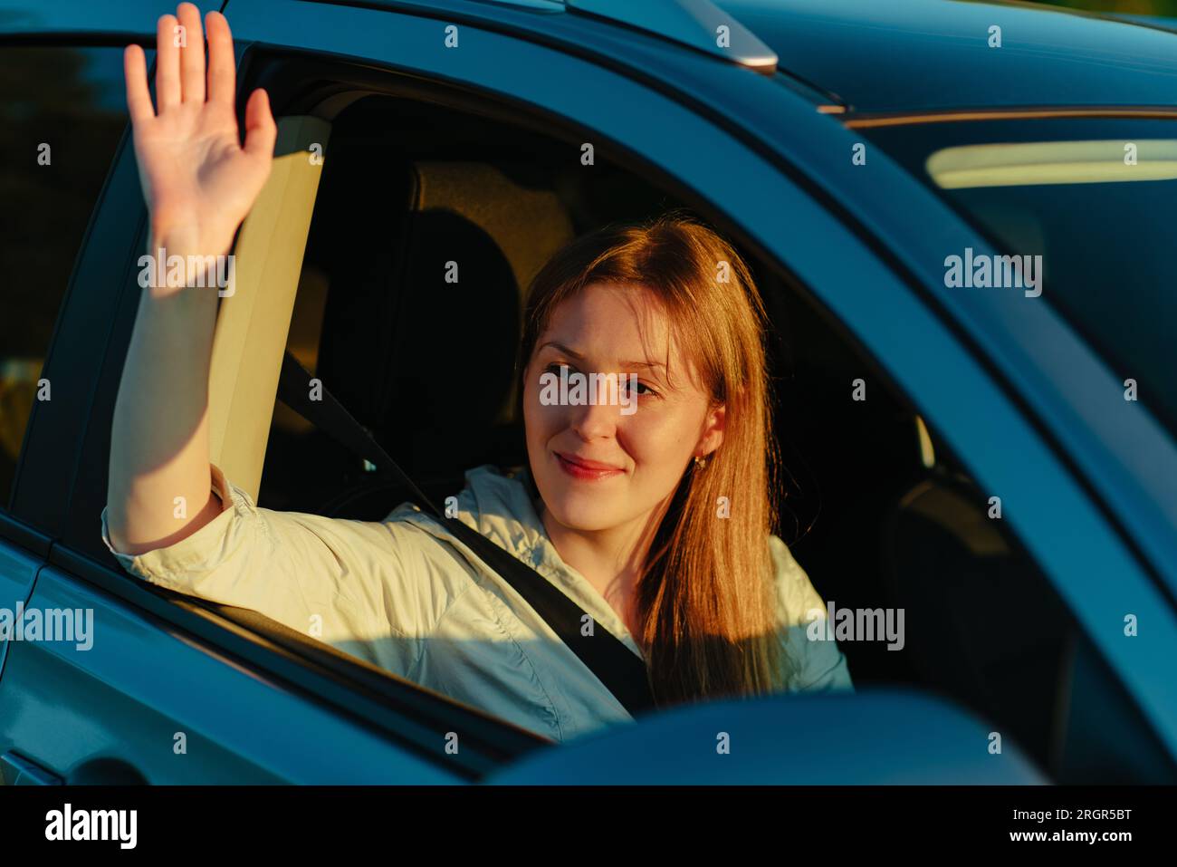 Happy young woman waving hand from car window Stock Photo - Alamy