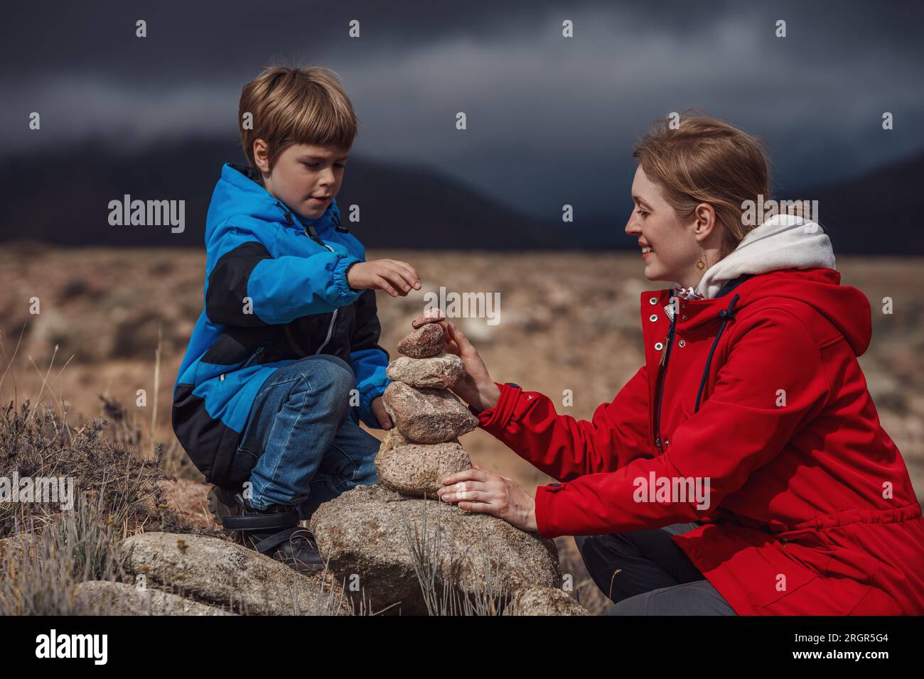 Young woman with her son build a pyramid of stones in the mountains ...