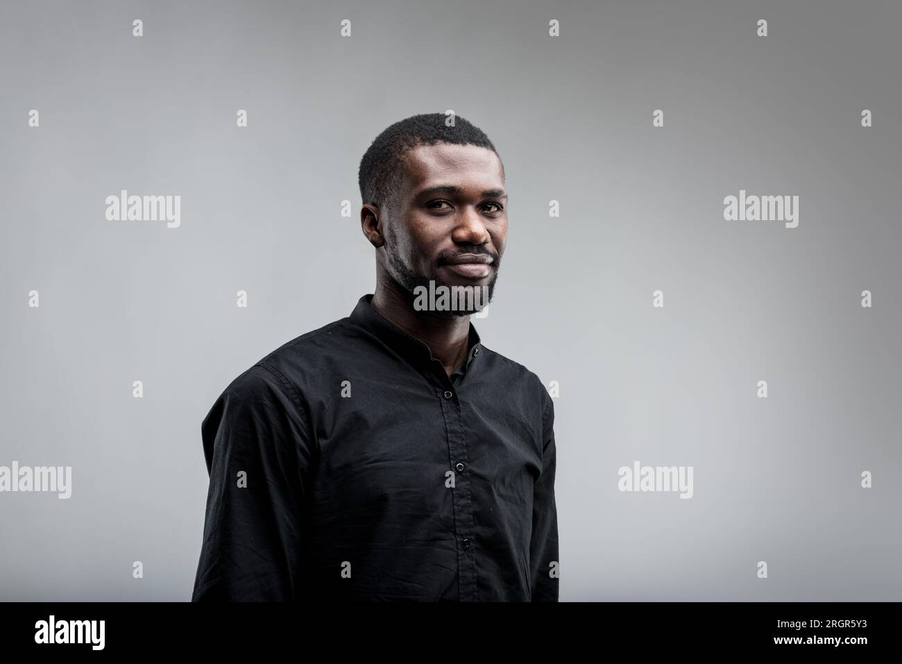 Three-quarter view of a black man, grey background, slight smile. Neat ...