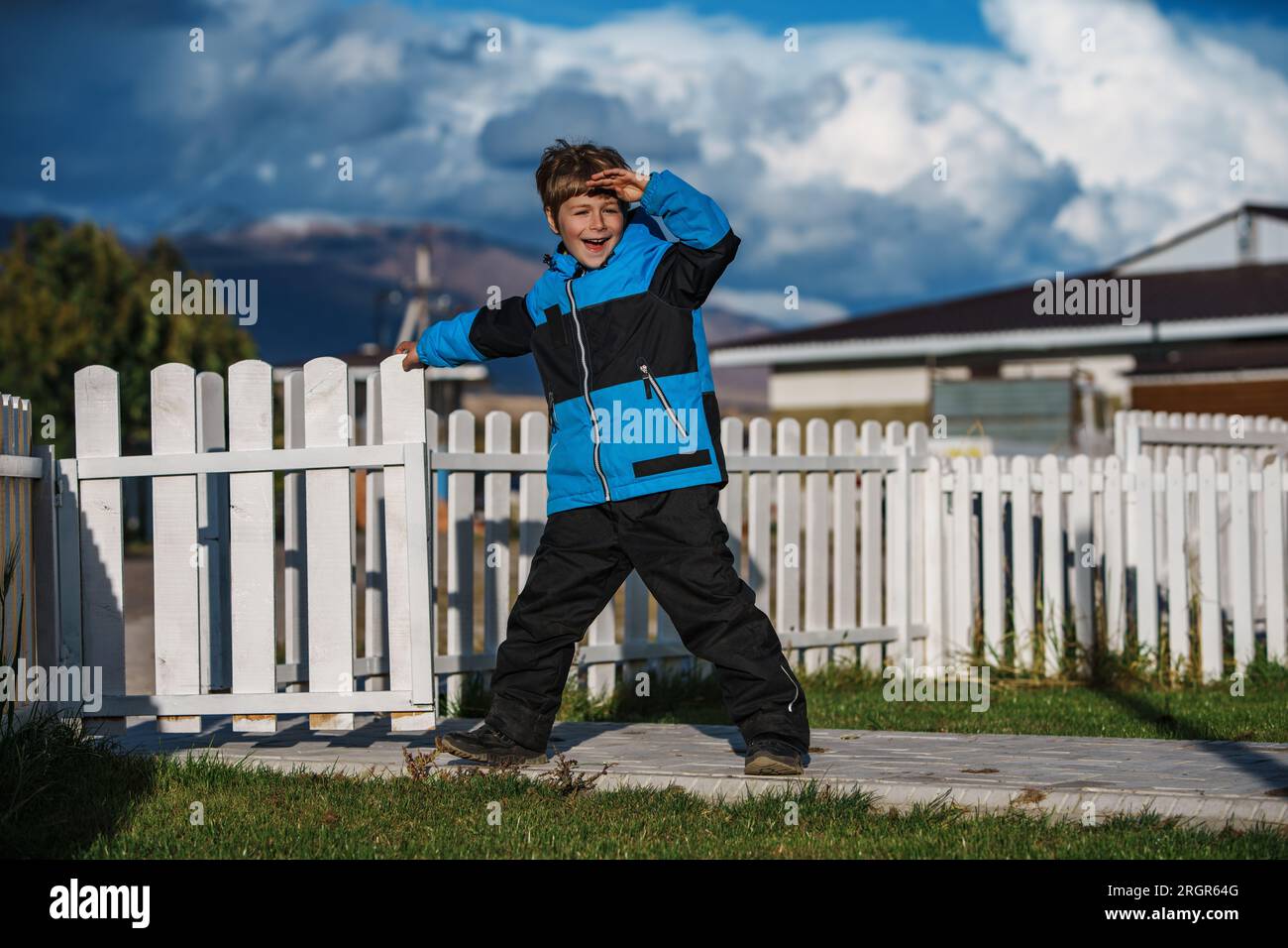 Boy in the yard of a country house looks into the distance and smiles ...