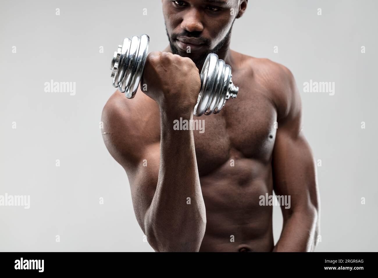 cool young black man lifts a shiny chrome weight. Defined chest and abs ...