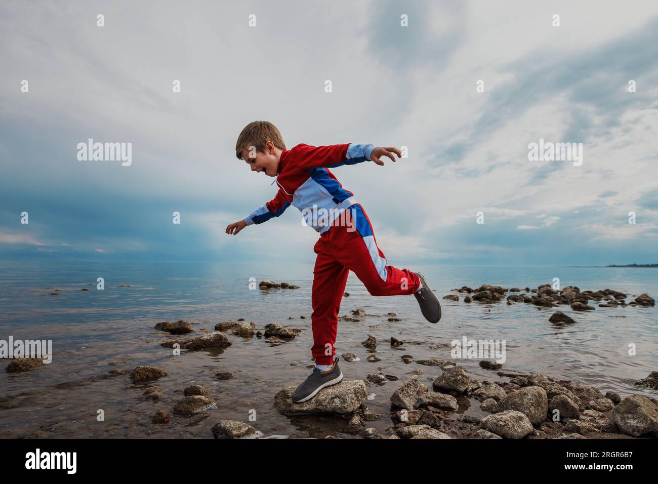Boy balancing on rock on the lake shore Stock Photo - Alamy
