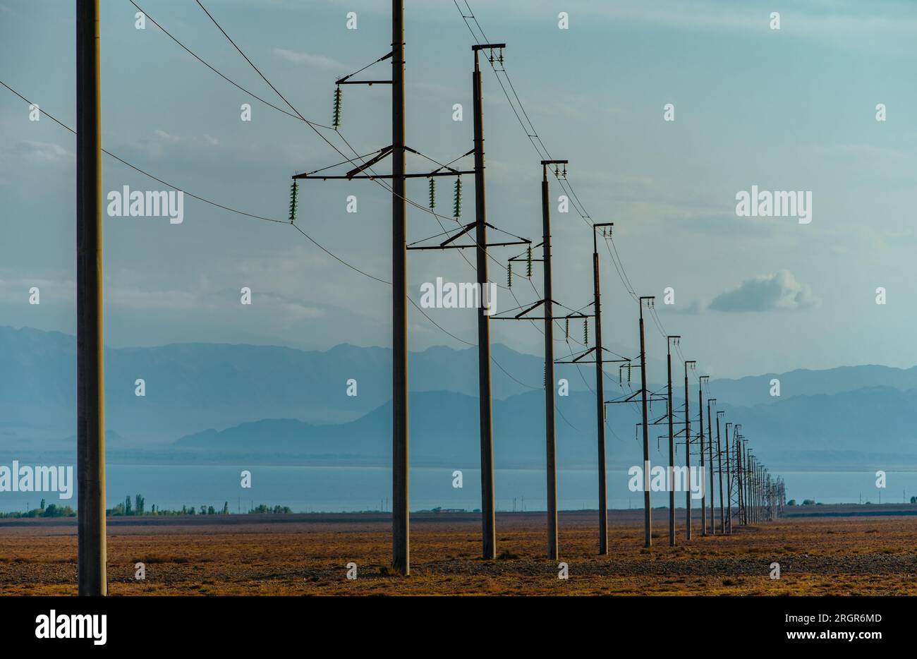 Electric power lines in field on mountains and lake background Stock ...