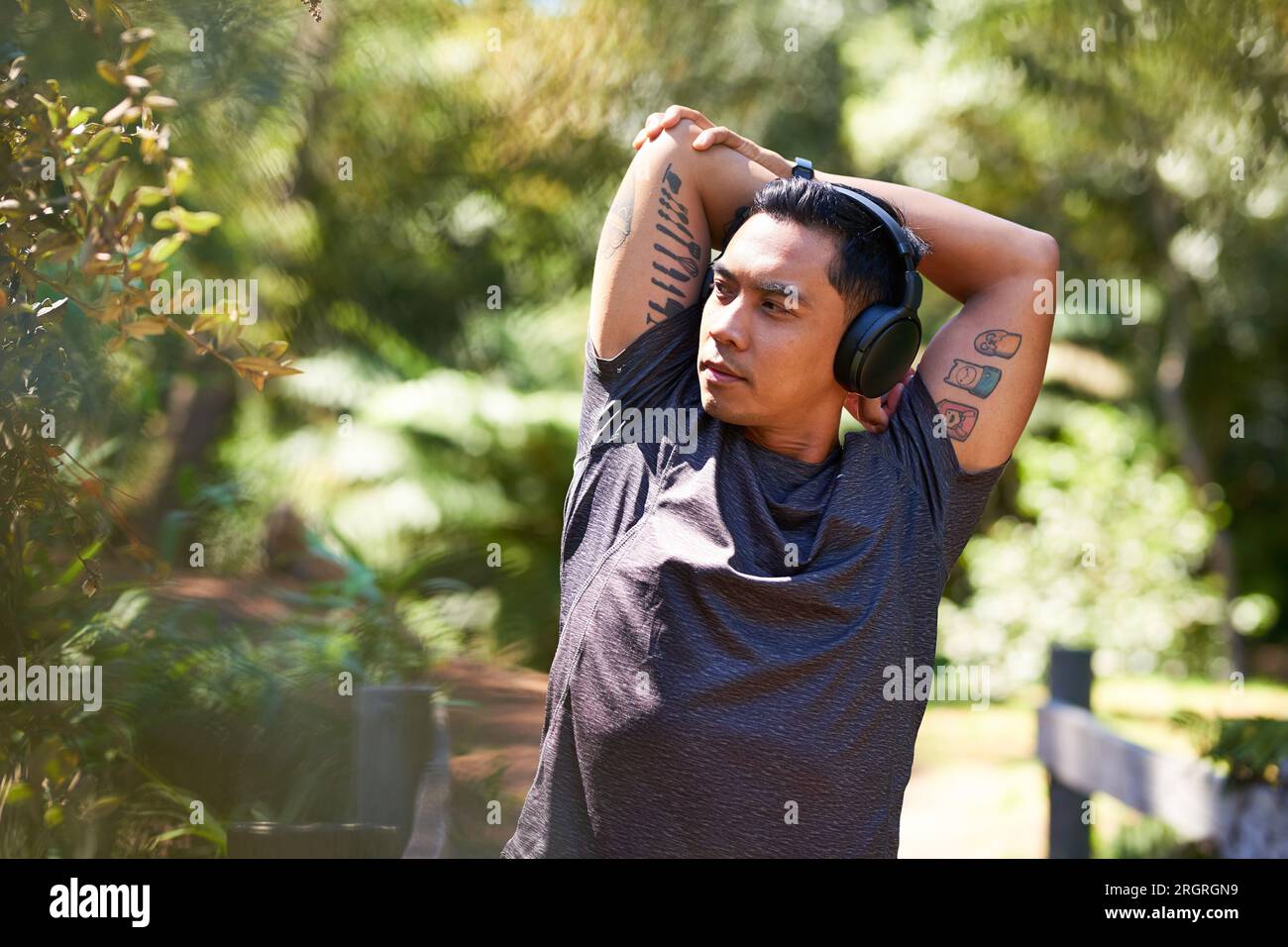 Serious Asian man stretches arms overhead for running warm up in park ...