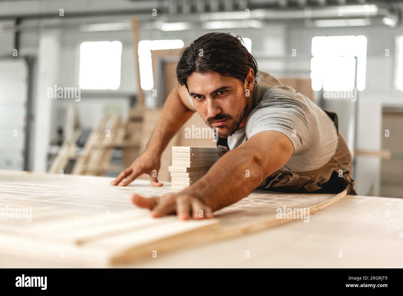 Young carpenter man looking and choosing wood plank at workshop in ...