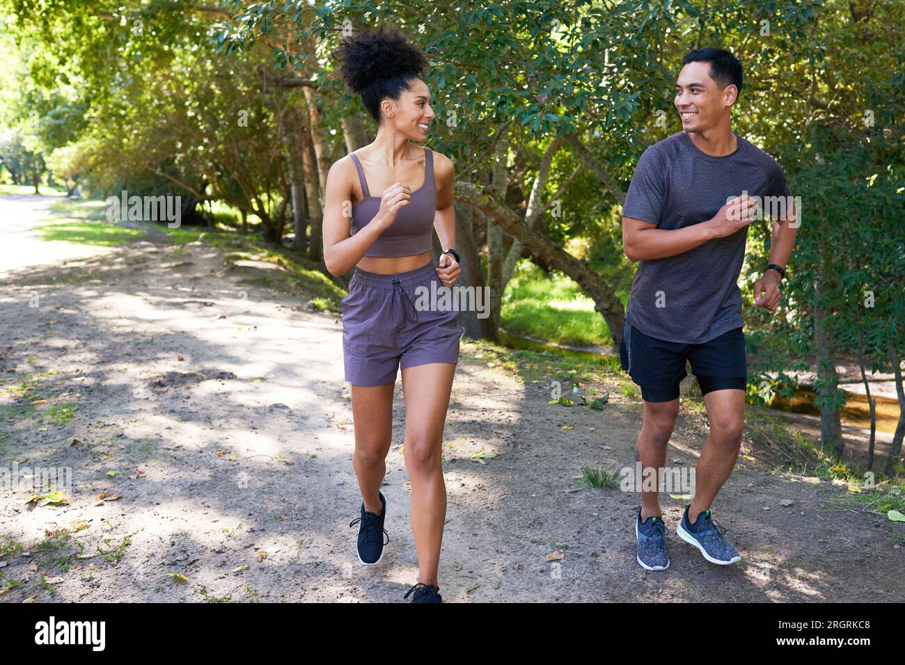 Fit couple runs together in park, trail running outdoors smiling and ...